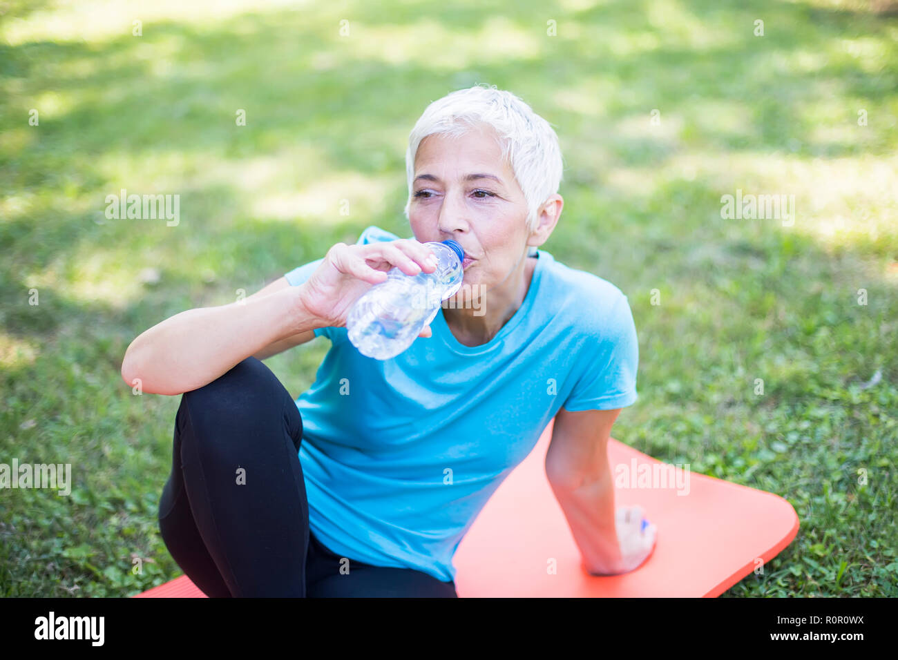 Senior sportive woman sitting on mat outside and resting after workout ...