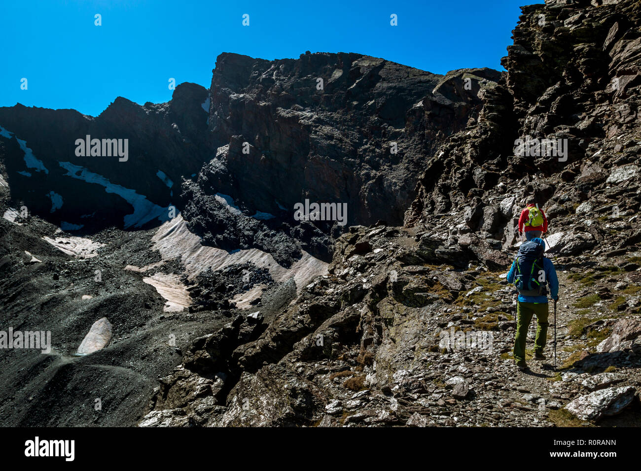 Back view of two travelers climbing up narrow mountain path on amazing ...