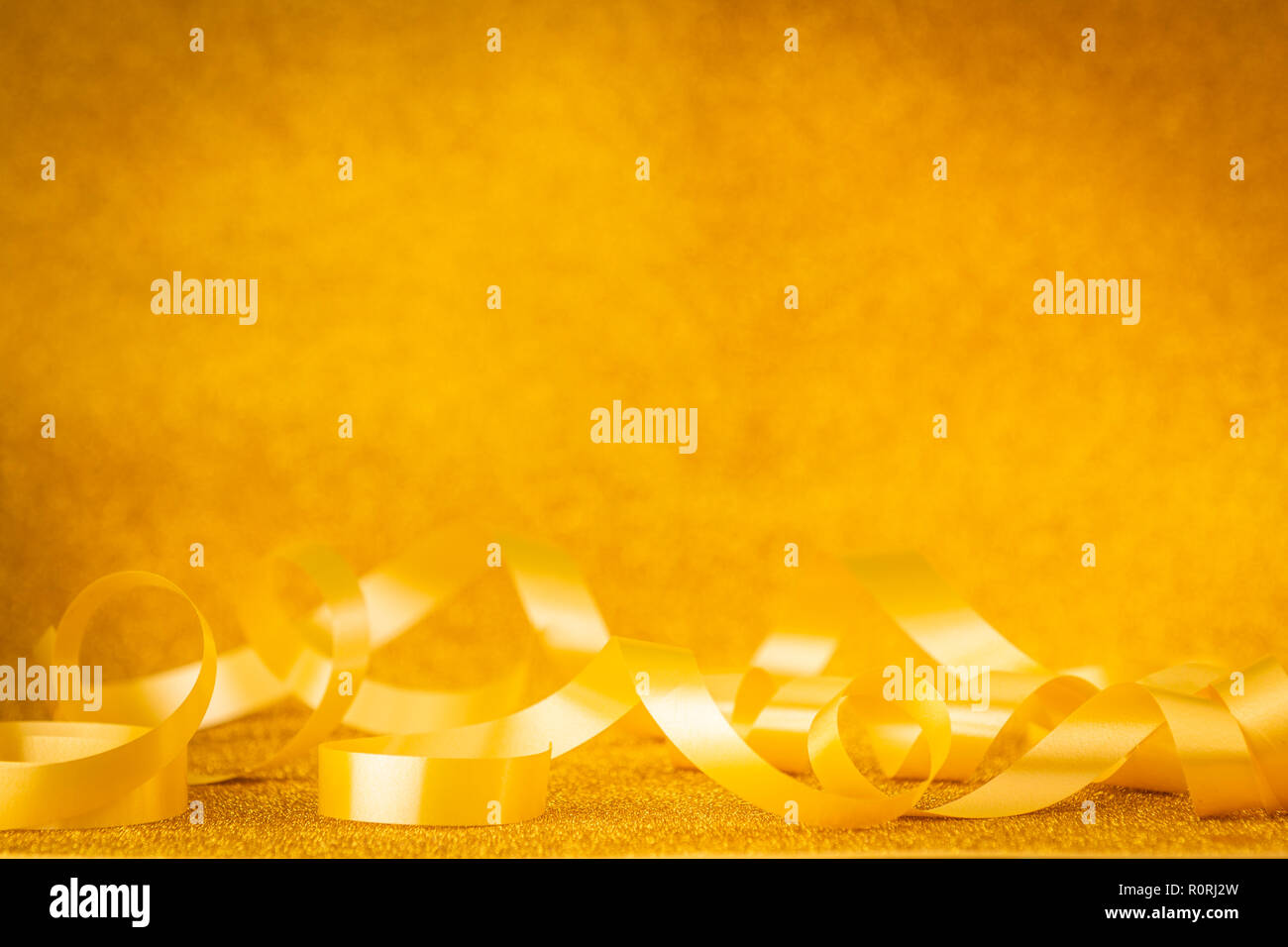 Curly yellow ribbon on golden glittering background Stock Photo - Alamy