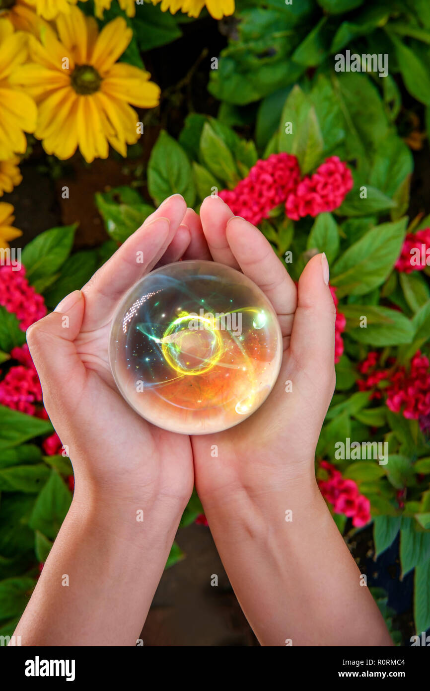 Female hands hold crystal ball atomic particle with flowers in ...