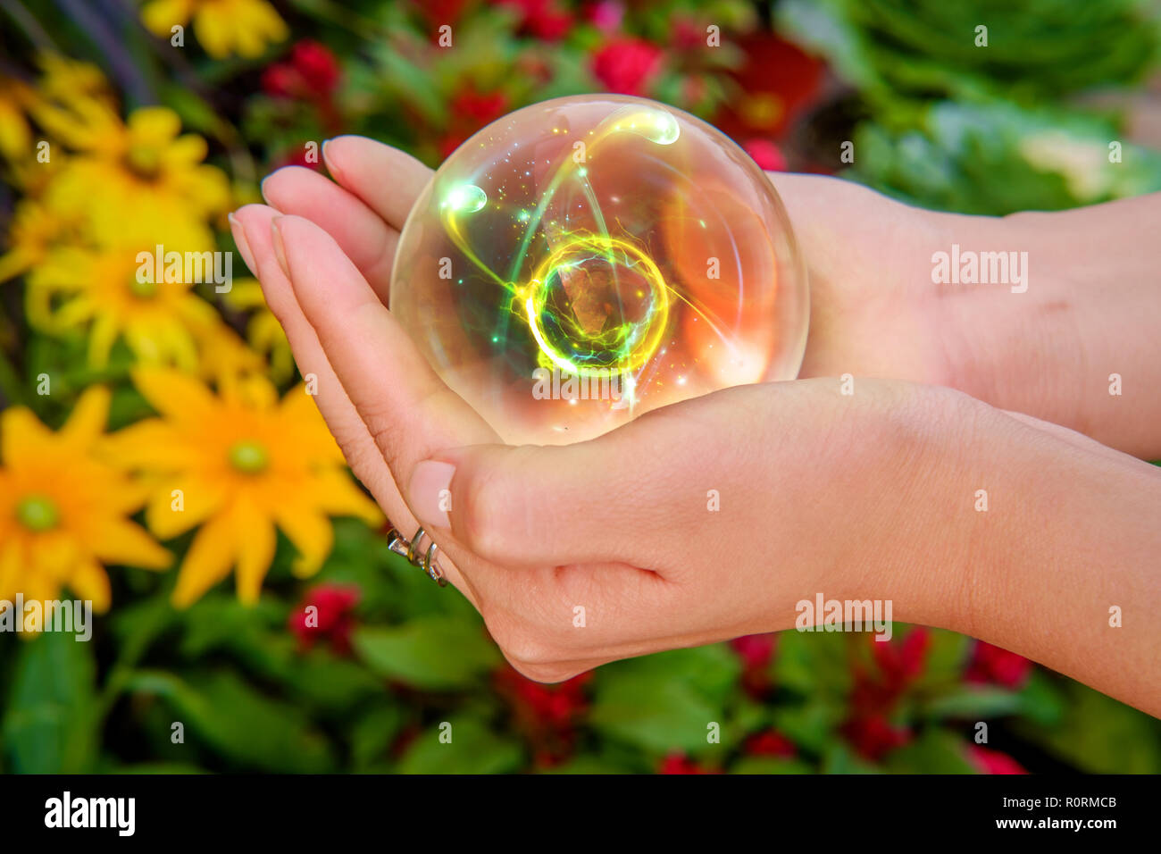Female hands hold crystal ball atomic particle with flowers in ...