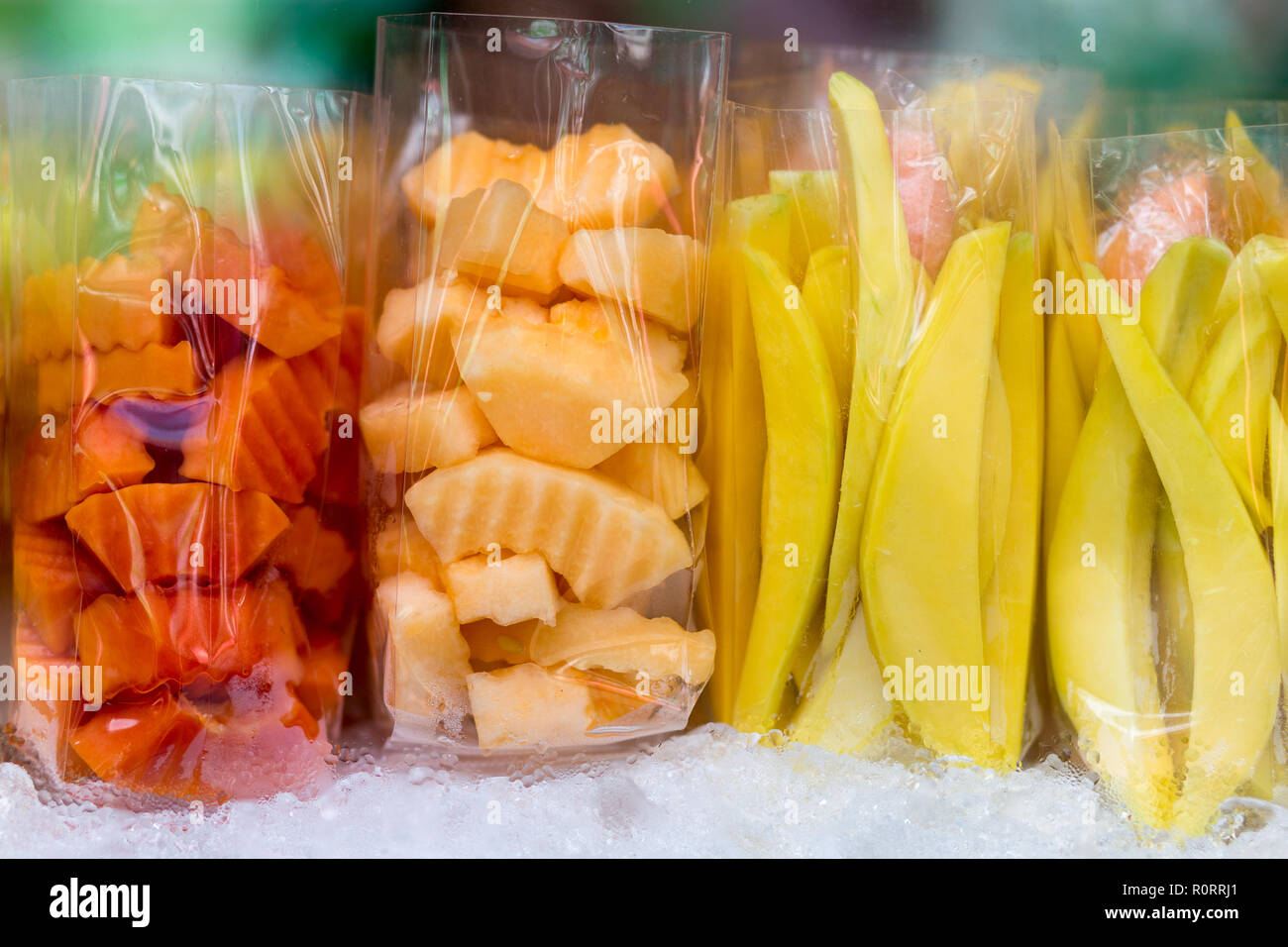 Fresh mango, melon and papaya fruits sliced in plastic bags in a street ...