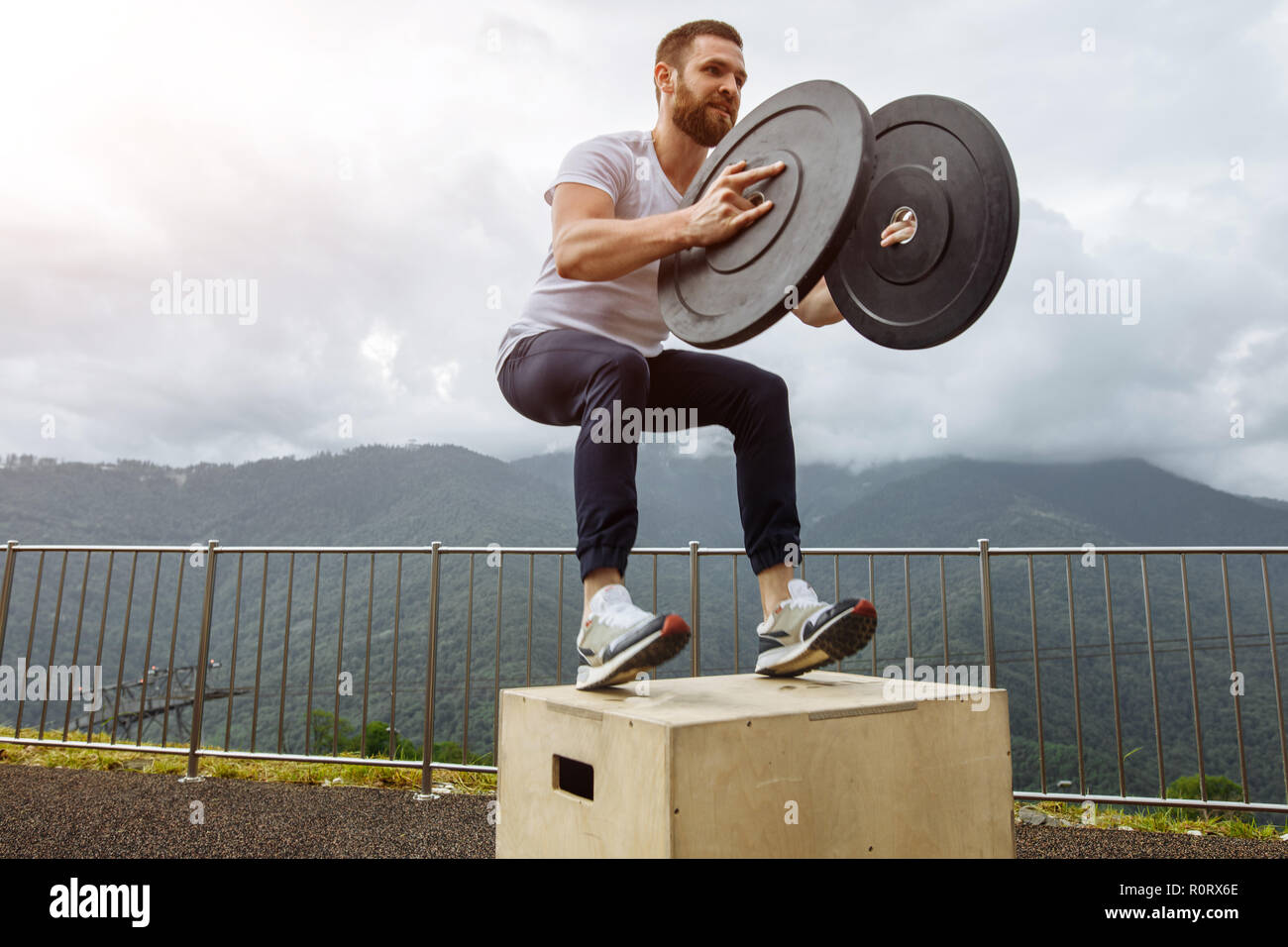 Strong male athlete doing box jumps with two plates outdoor on top of ...