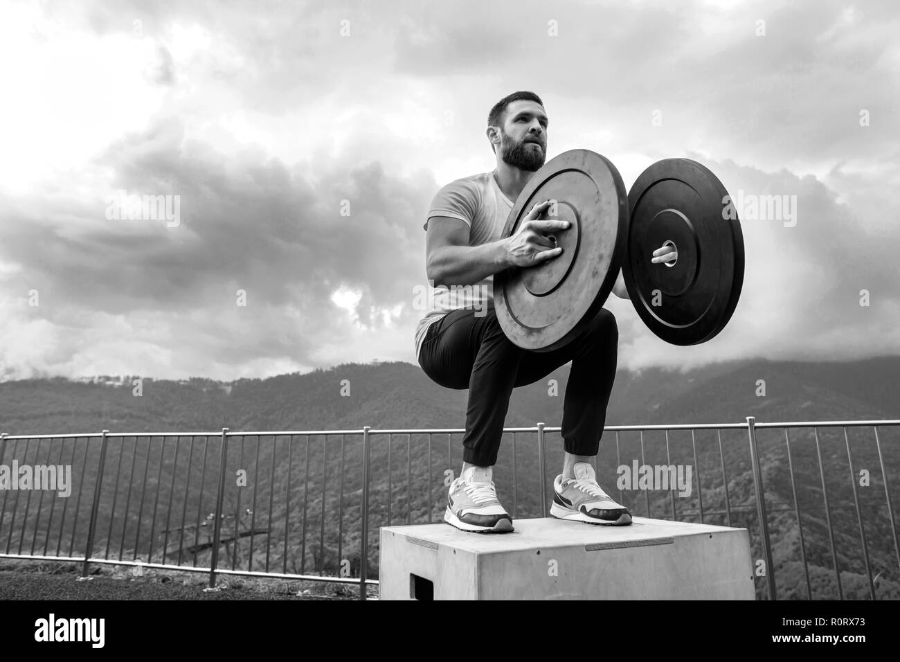 Strong male athlete doing box jumps with two plates outdoor on top of ...