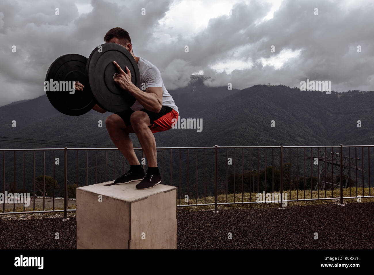 Strong male athlete doing box jumps with two plates outdoor on top of ...