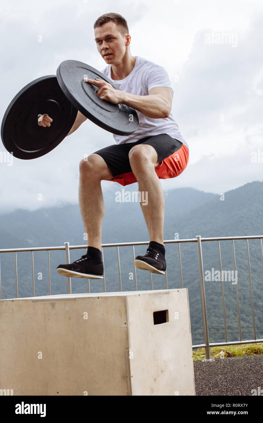 Strong male athlete doing box jumps with two plates outdoor on top of ...