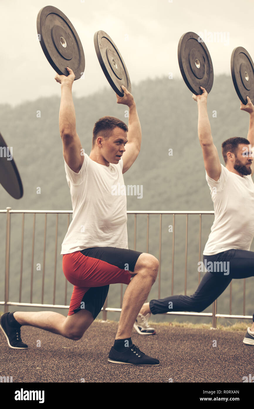 two athletes with barbell disc making lunges in outdoor workout Stock ...