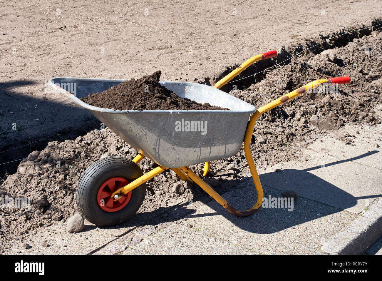 Wheelbarrow with soil parked on pavement by a narrow ditch Stock Photo ...