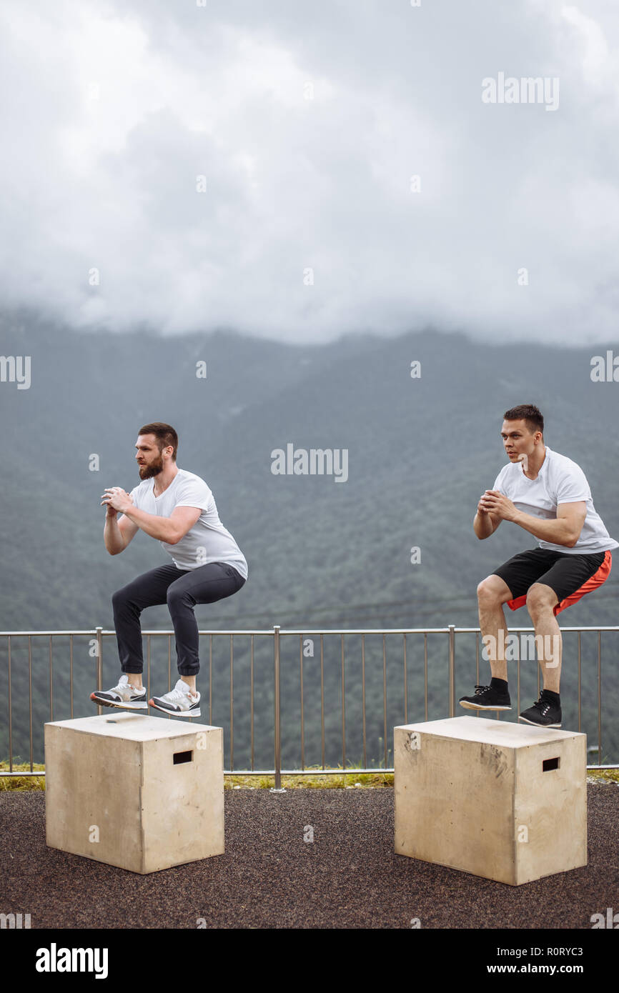 Two male athletic friends doing box jump outdoor on top of the mountain ...