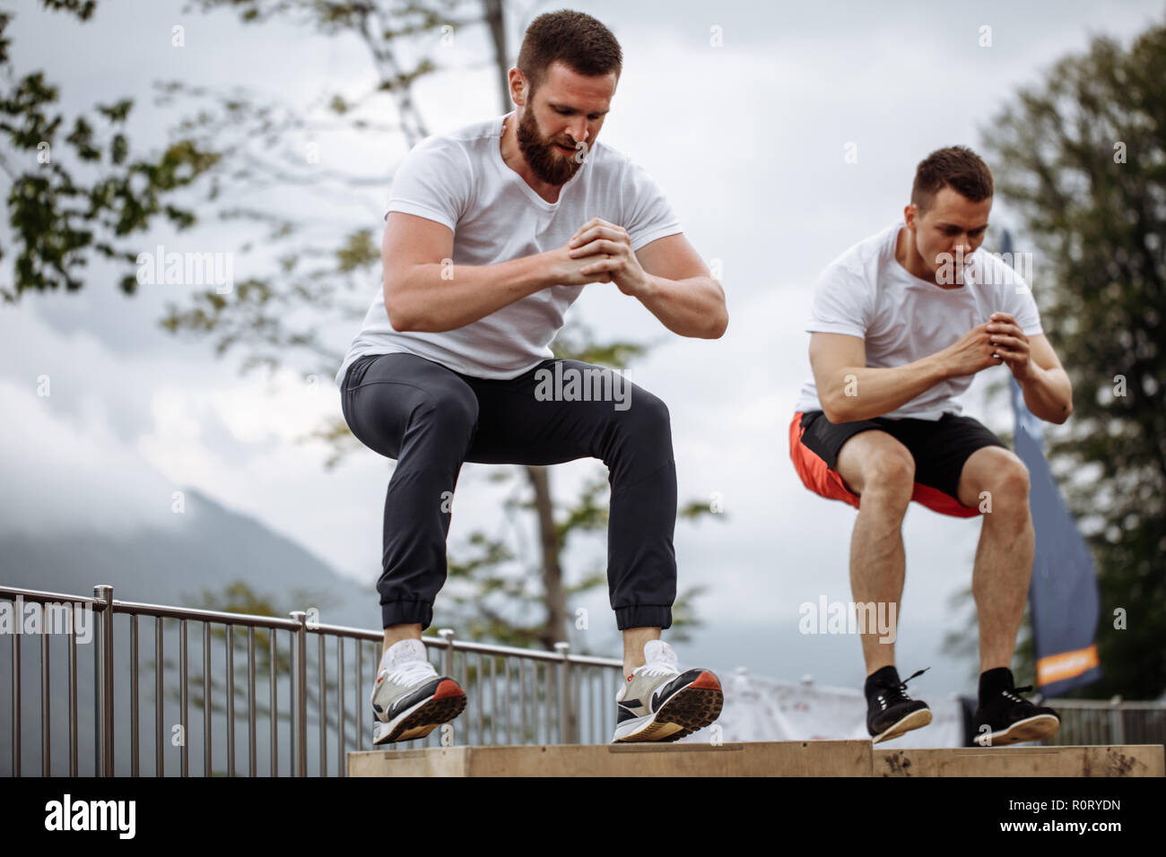 Two male athletic friends doing box jump outdoor on top of the mountain ...