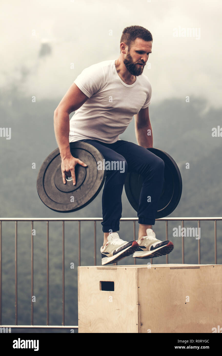 Strong male athlete doing box jumps with two plates outdoor on top of ...