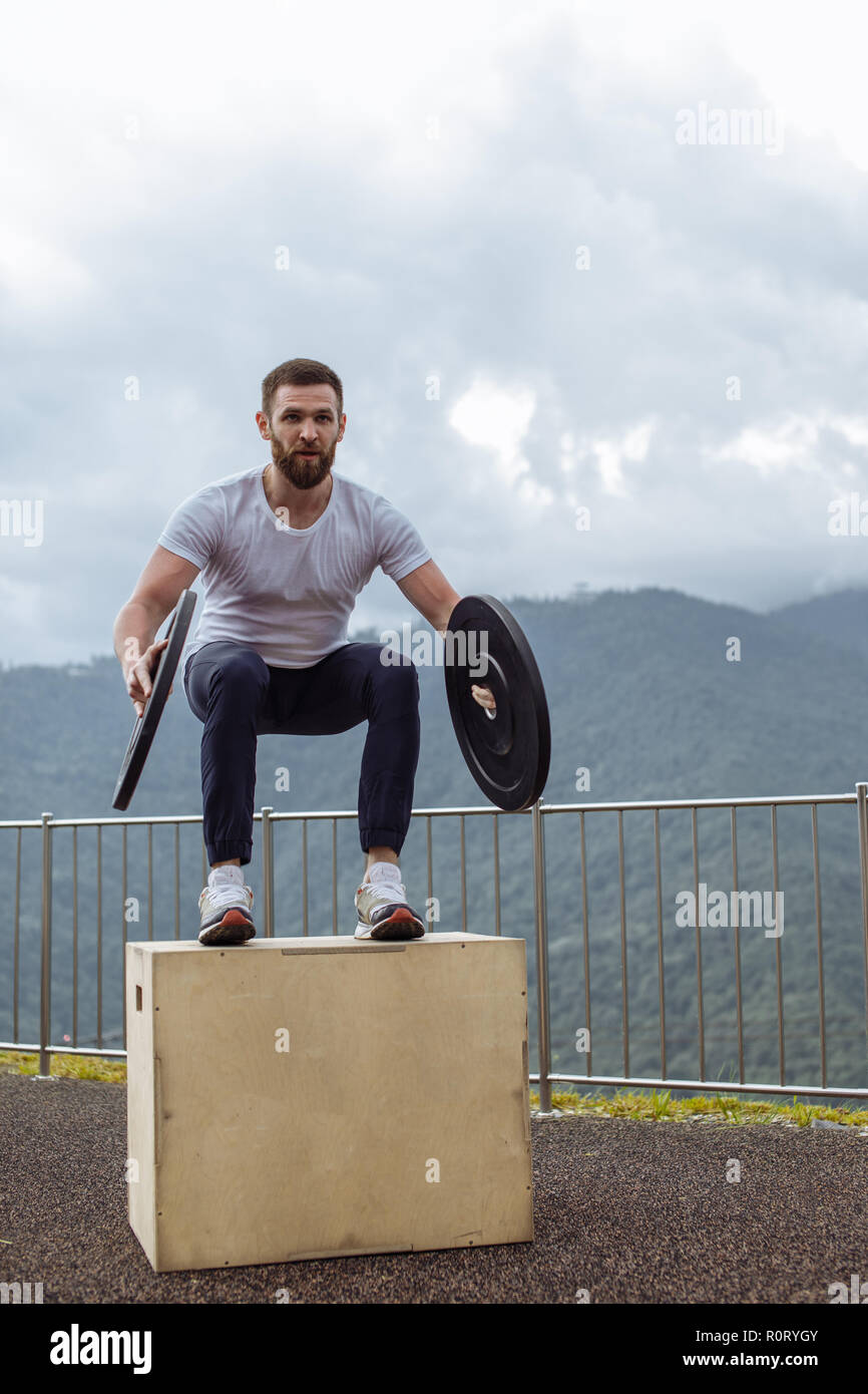 Strong male athlete doing box jumps with two plates outdoor on top of ...