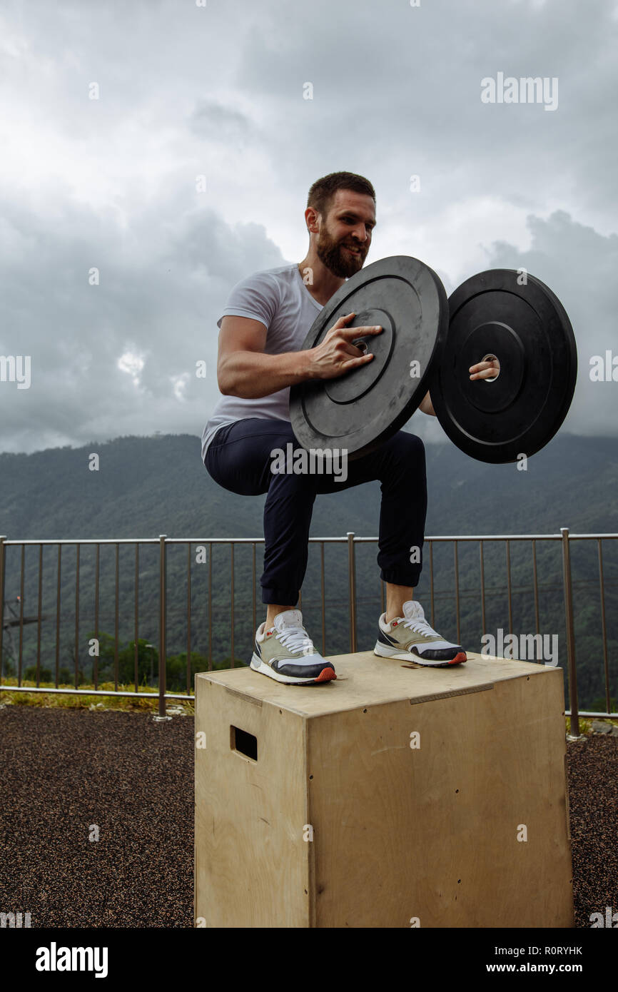Strong male athlete doing box jumps with two plates outdoor on top of ...