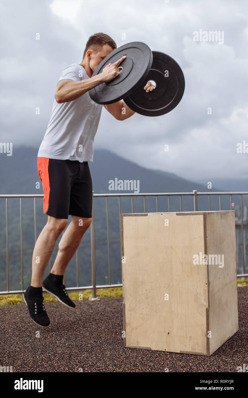 Strong male athlete doing box jumps with two plates outdoor on top of ...