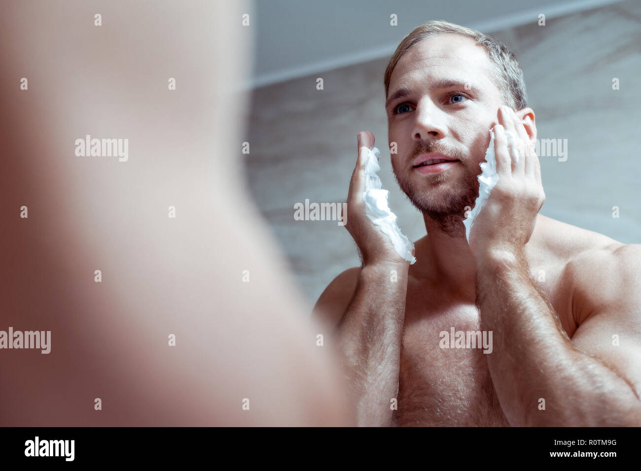 Blue-eyed man with nice muscle body shaving his face in the morning ...