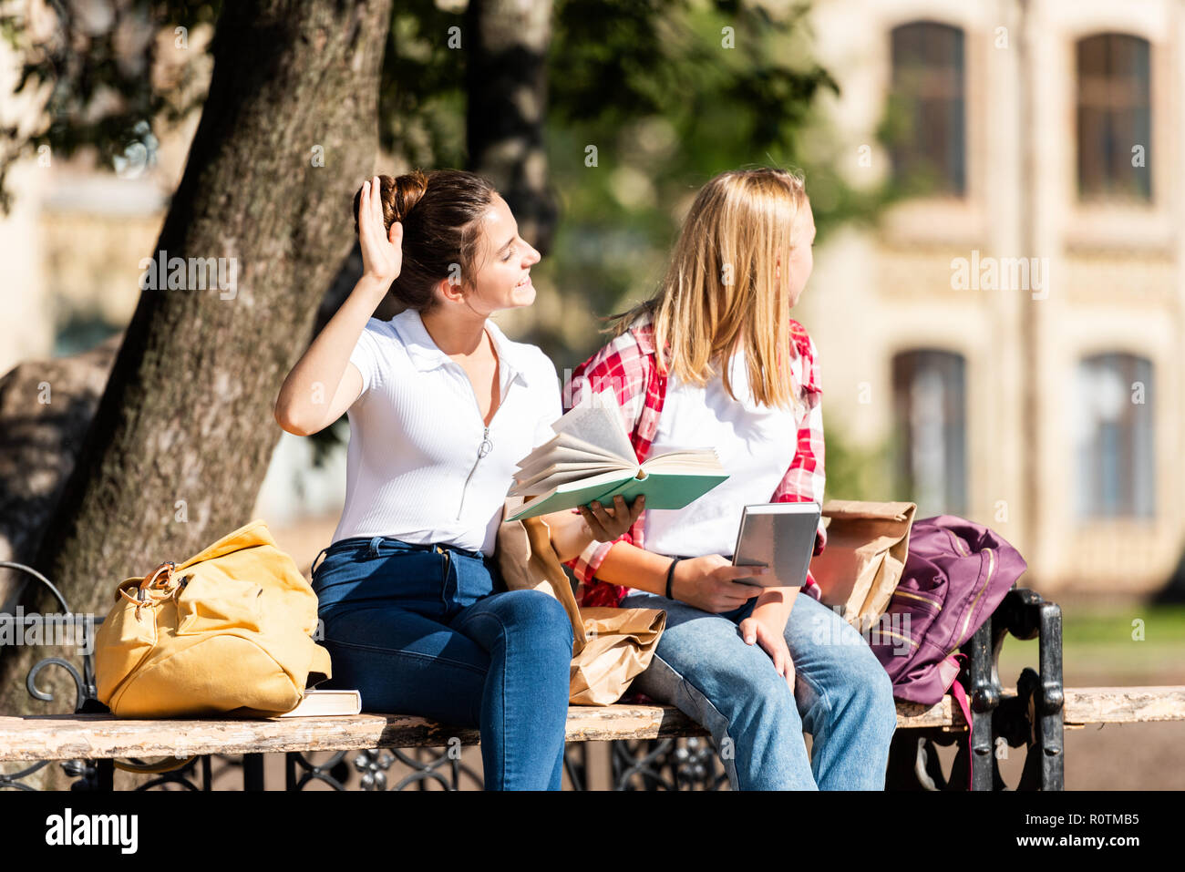 teen schoolgirls sitting on bench and reading homework together Stock ...