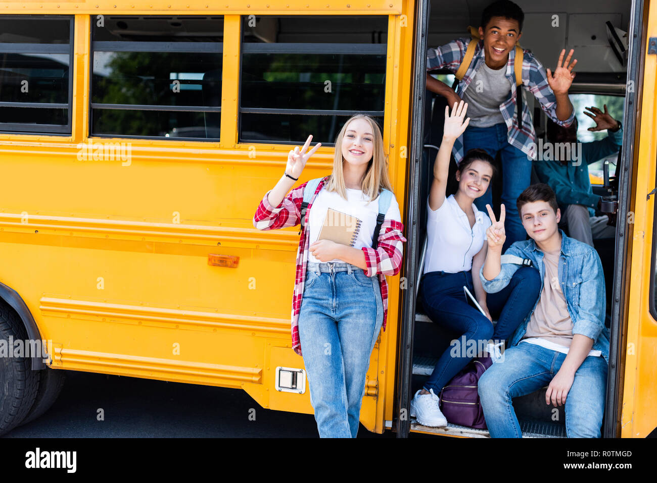 group of teen scholars sitting at school bus with driver inside and ...