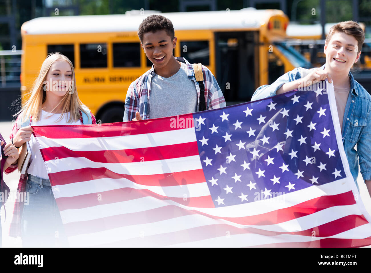 group of smiling teen students holding usa flag in front of school bus ...