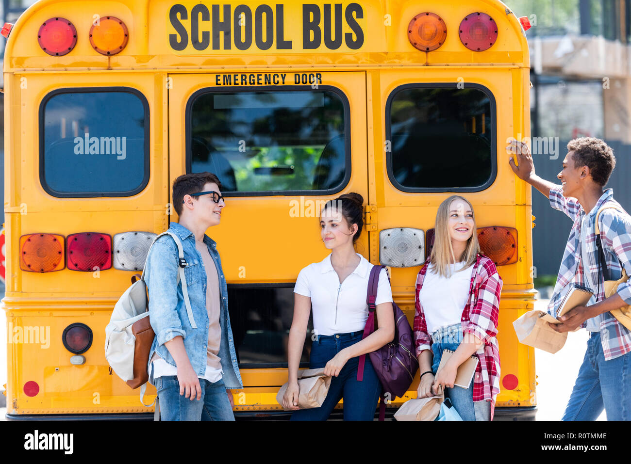 group of teen scholars chatting while leaning on school bus Stock Photo ...