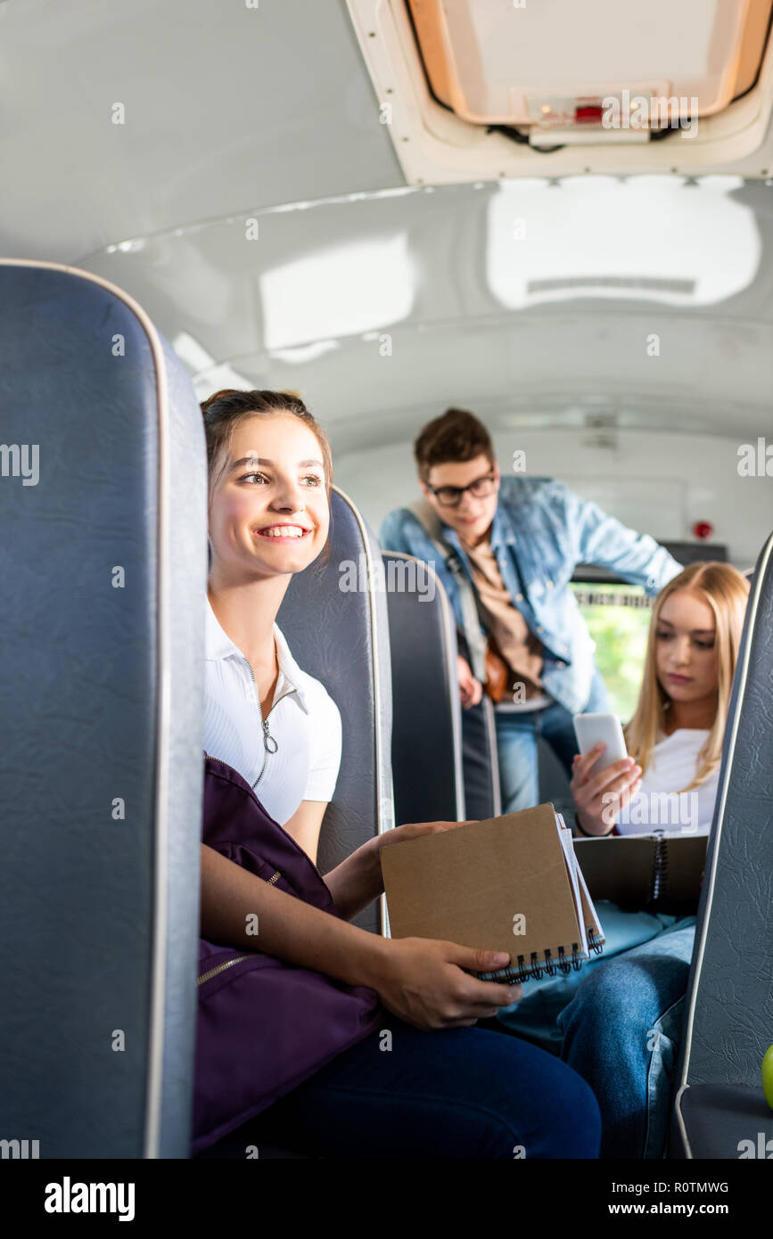 happy teen schoolgirl riding school bus with classmates and looking ...