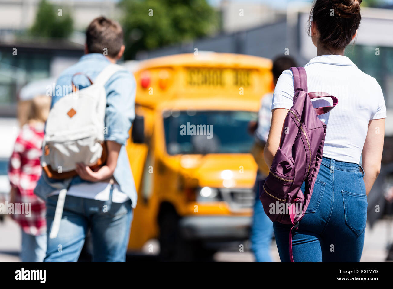 rear view of group of students with backpacks walking at school bus ...