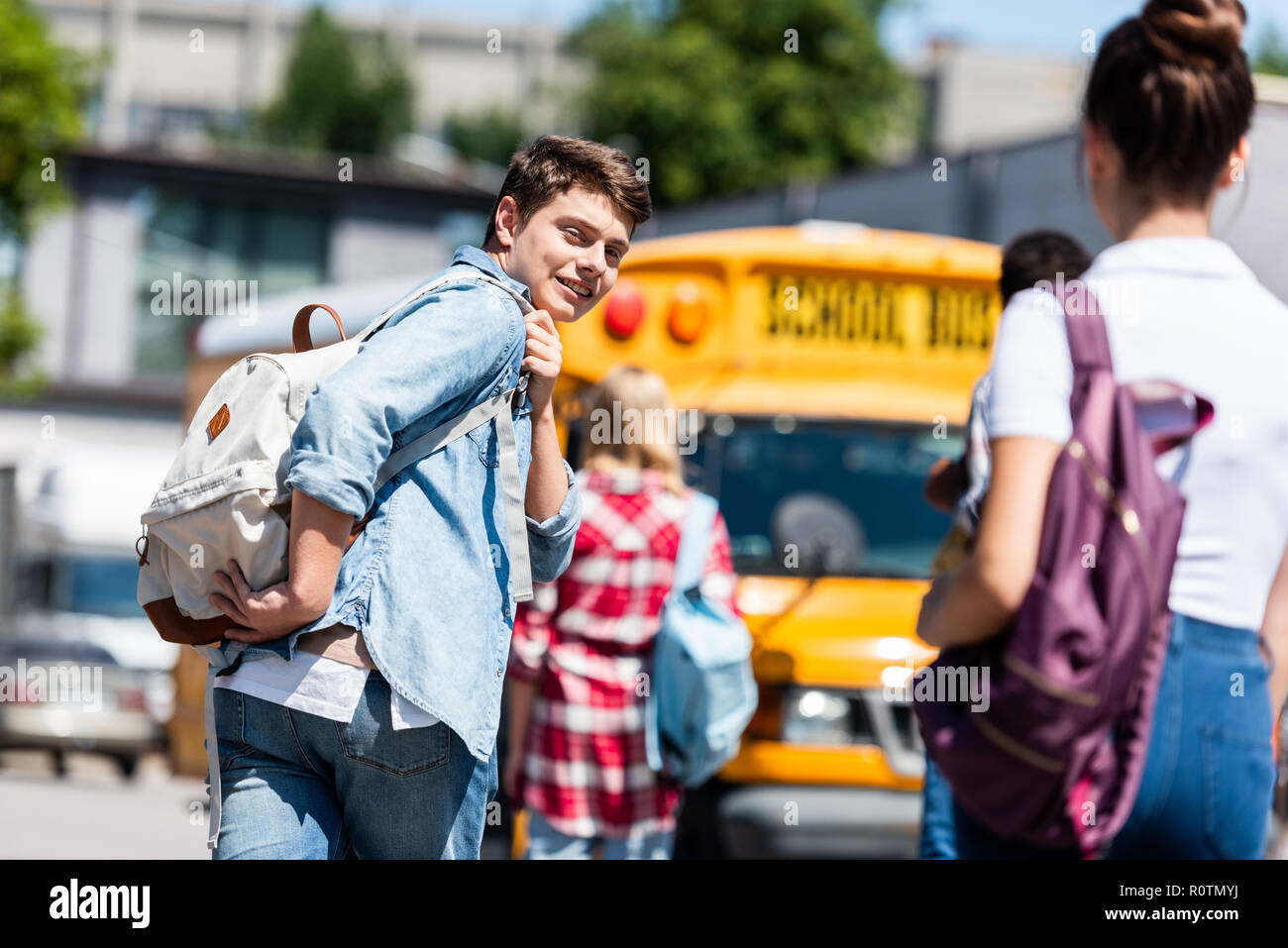 rear view of smiling teen schoolboy walking to school bus with his ...