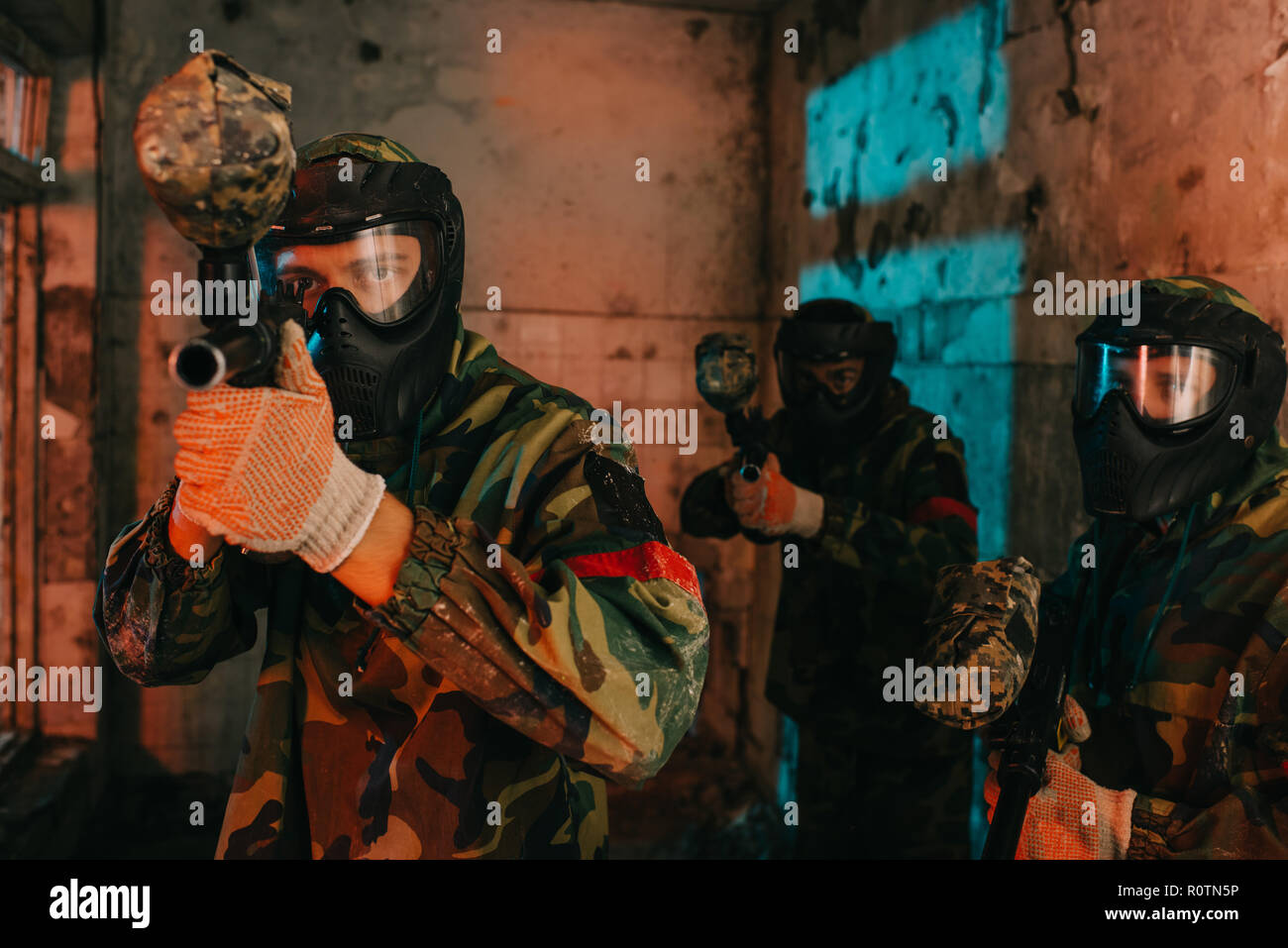 paintball team in uniform and protective masks playing paintball with ...