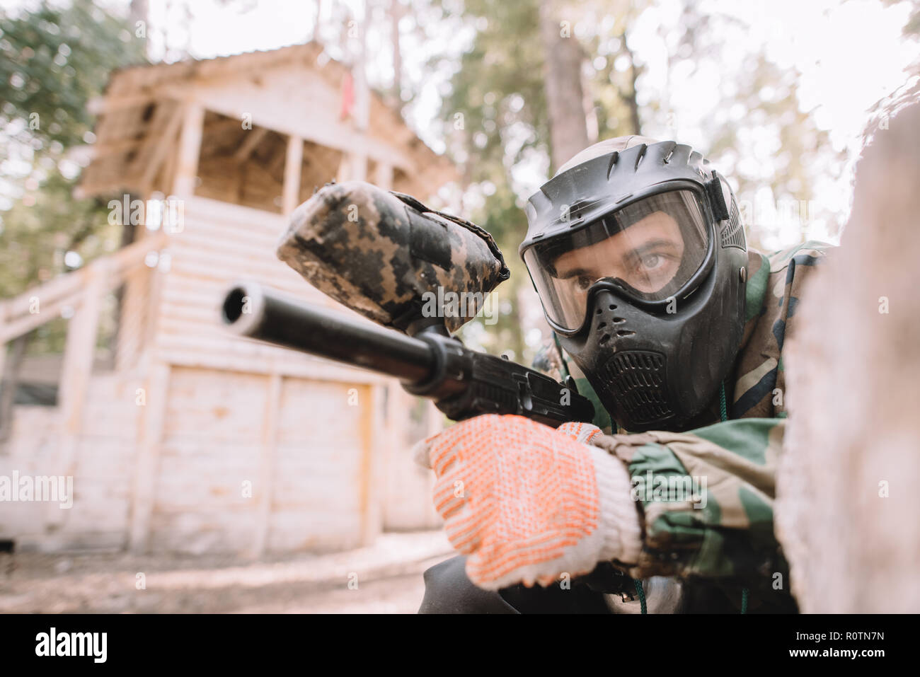 serious male paintball player in goggle mask and camouflage aiming by ...