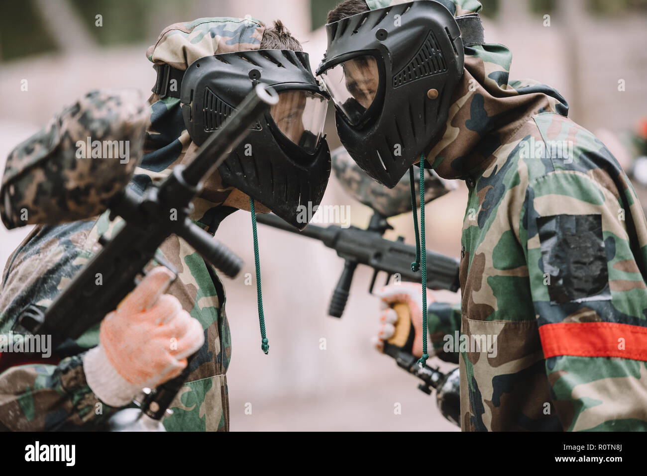 side view of male paintballers in protective masks and camouflage ...