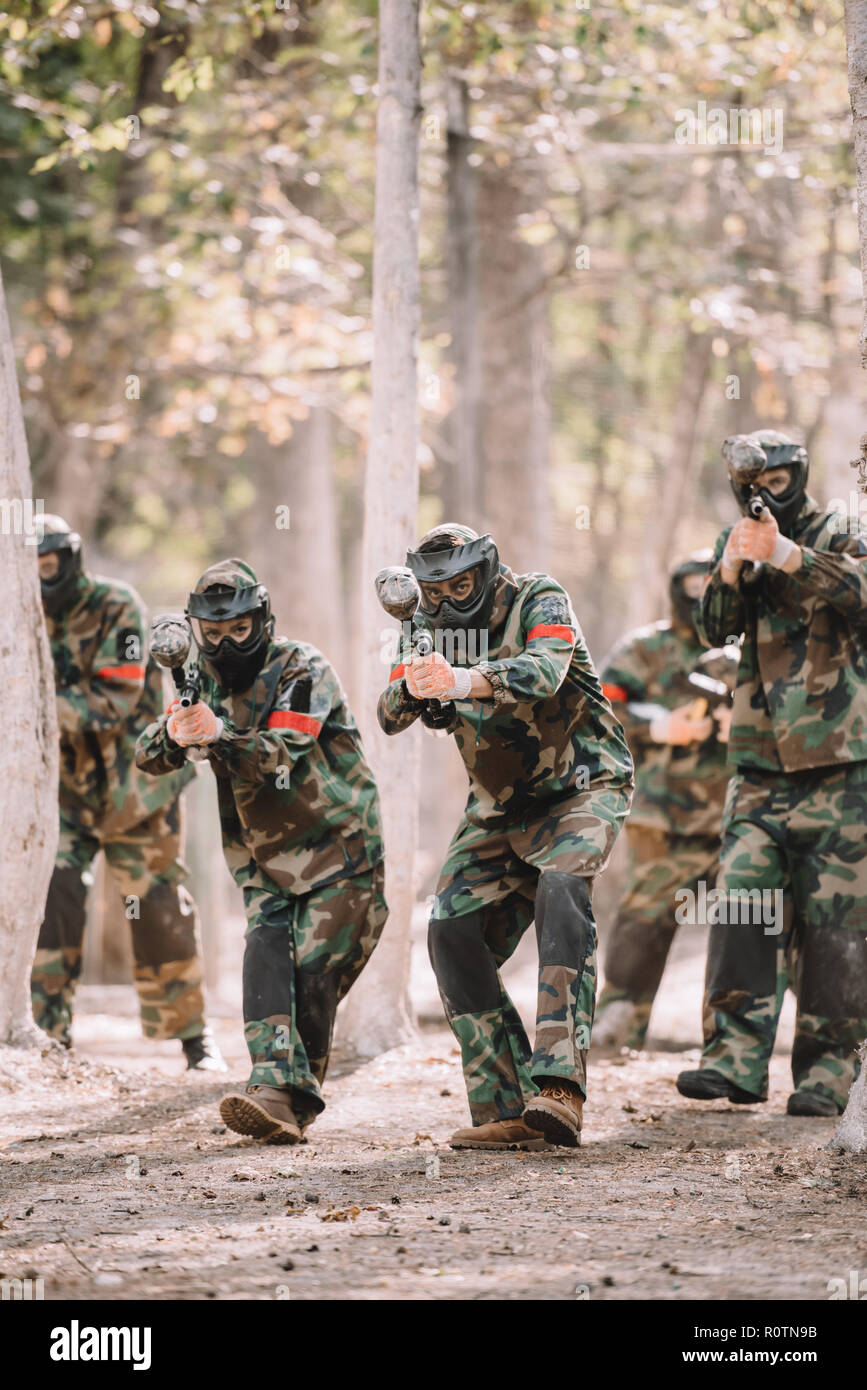 paintball team in uniform and protective masks running and aiming by ...