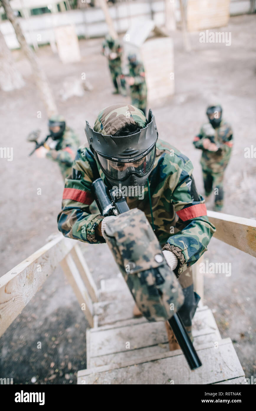 high angle view of paintball player aiming by marker gun and running on ...
