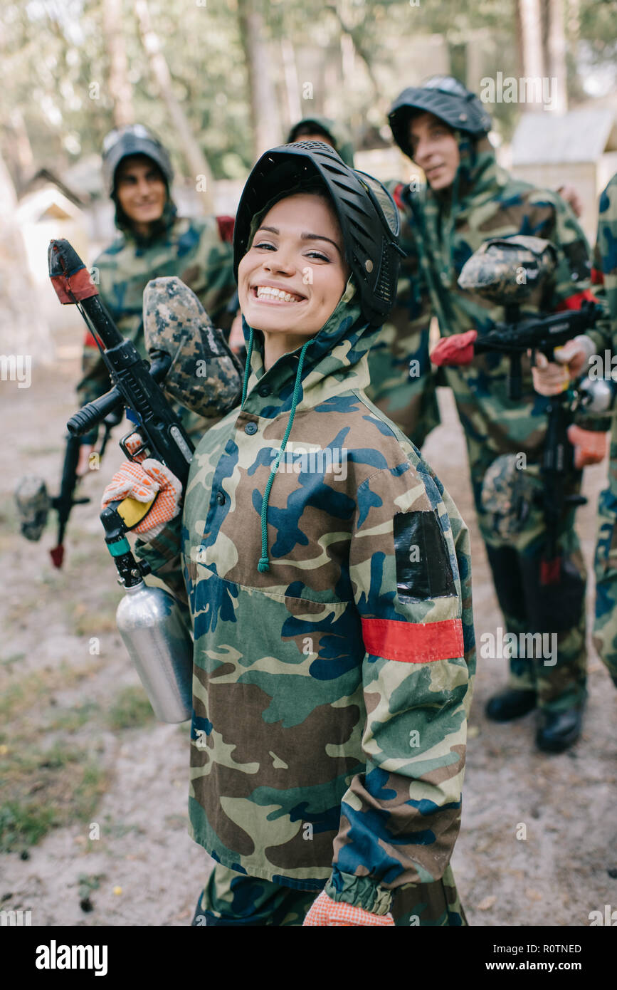 attractive smiling female paintballer in uniform holding paintball gun ...