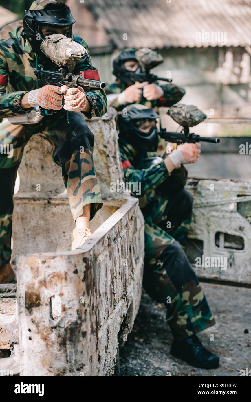 paintball players aiming with marker guns from broken car outdoors ...