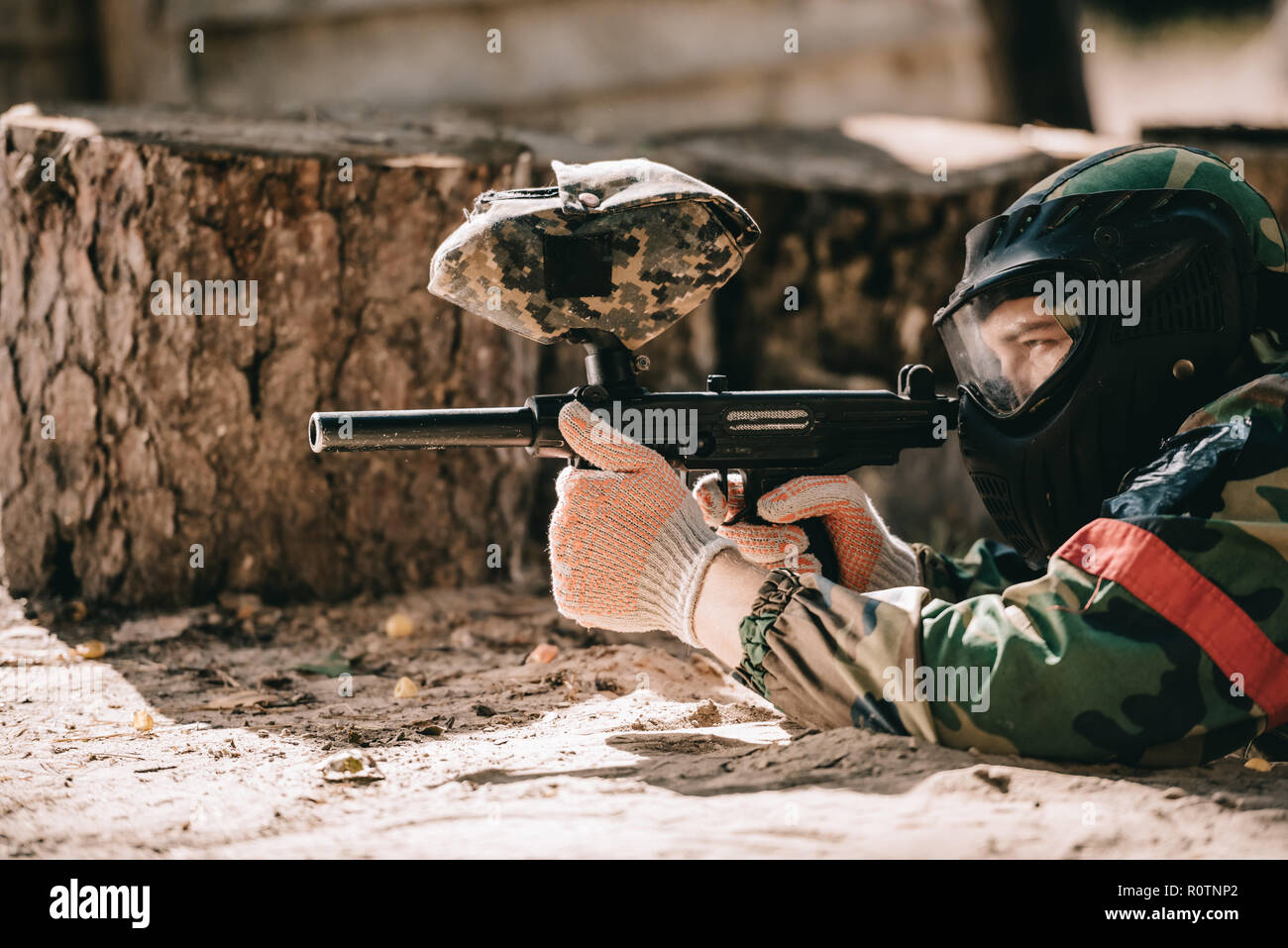 focused male paintball player in goggle mask and camouflage aiming by ...