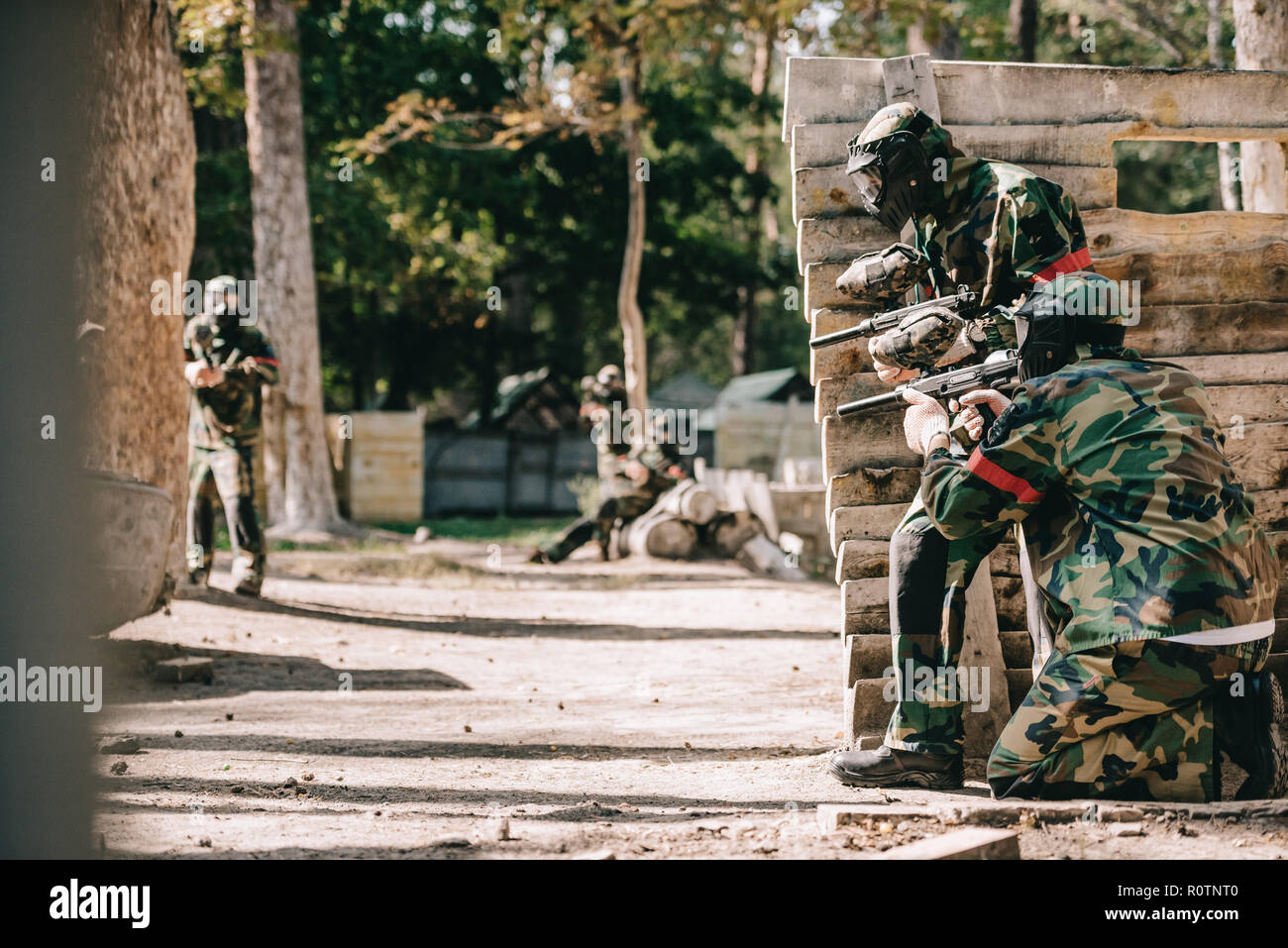 paintball players in camouflage and protective masks aiming with marker ...