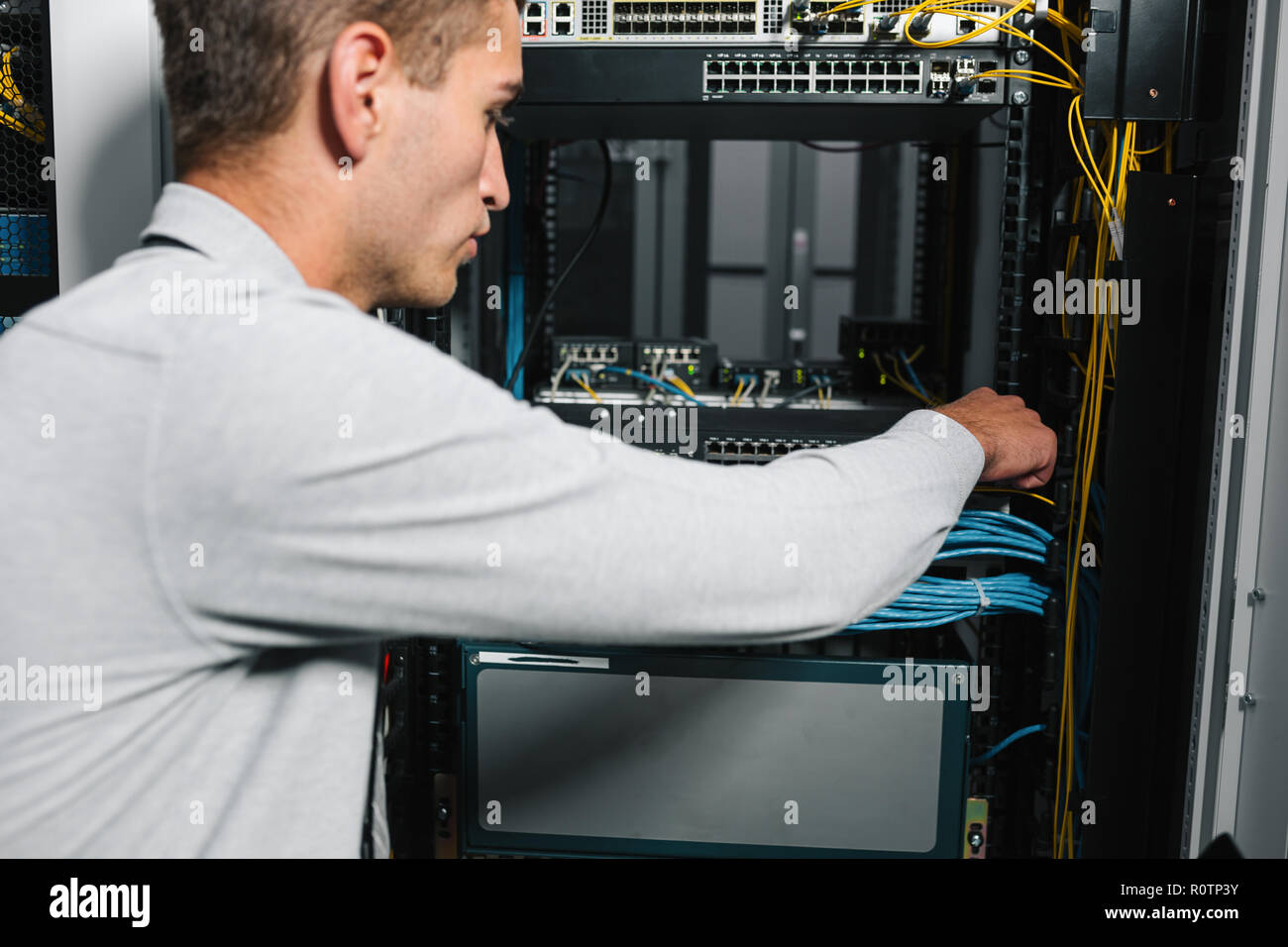young man connecting wires in server cabinet while working with ...