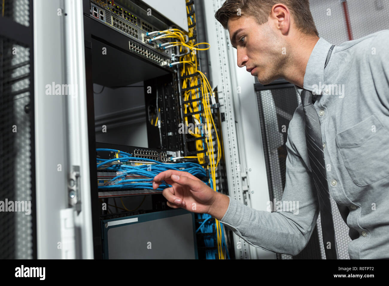 young man connecting wires in server cabinet while working with ...