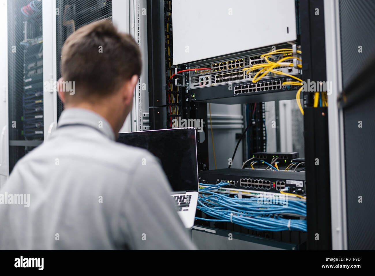 young man connecting wires in server cabinet while working with ...