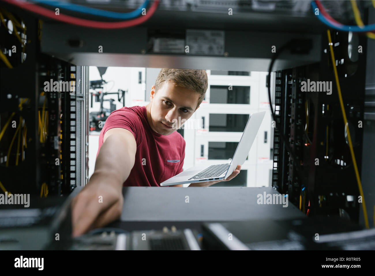 young man connecting wires in server cabinet while working with ...