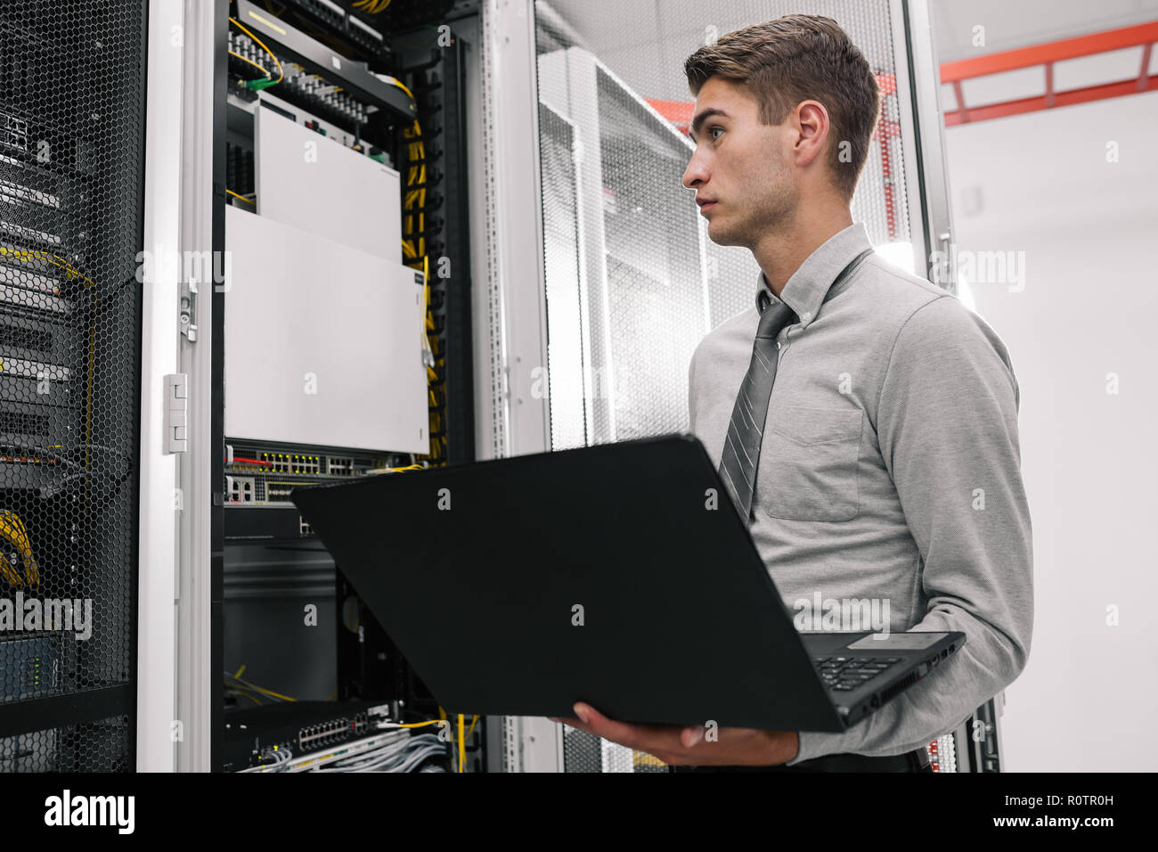 young man connecting wires in server cabinet while working with ...