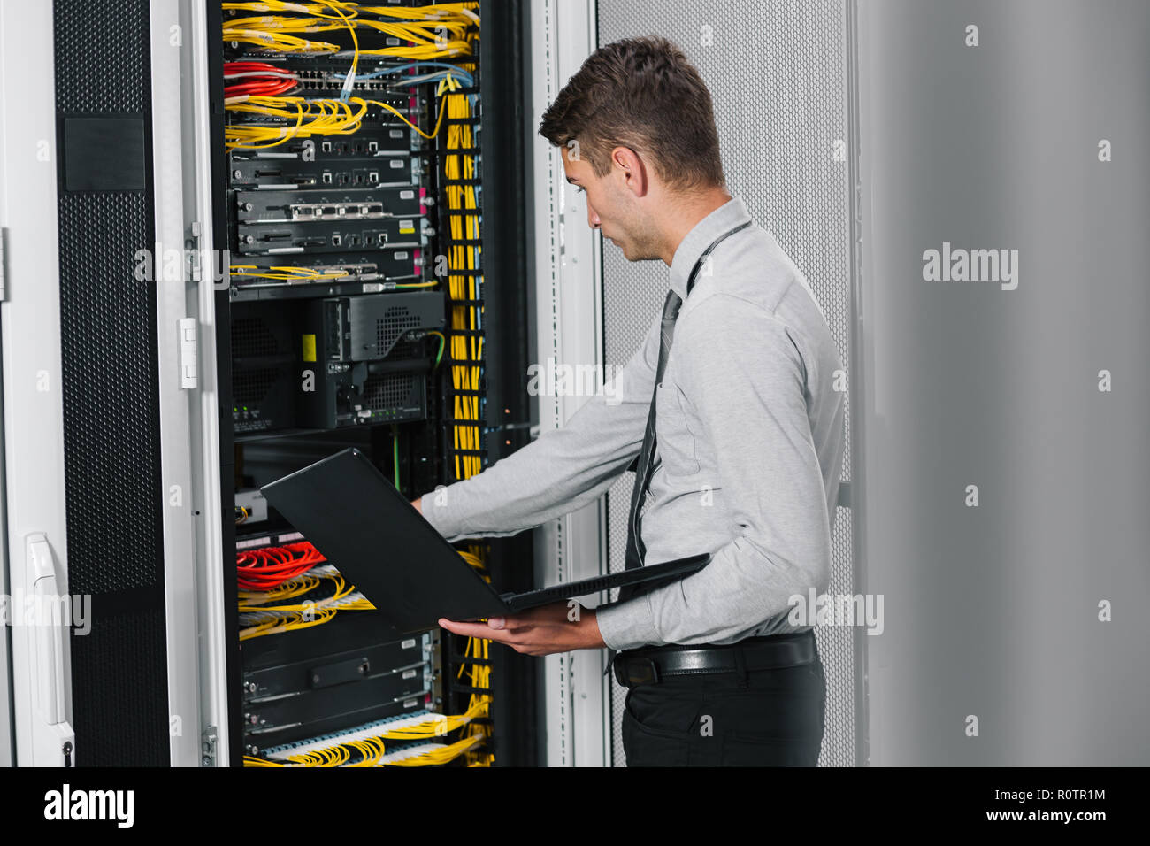 young man connecting wires in server cabinet while working with ...