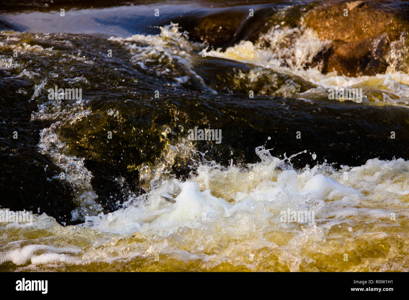 powerful stream of water goes around stone rapids with splashes and ...