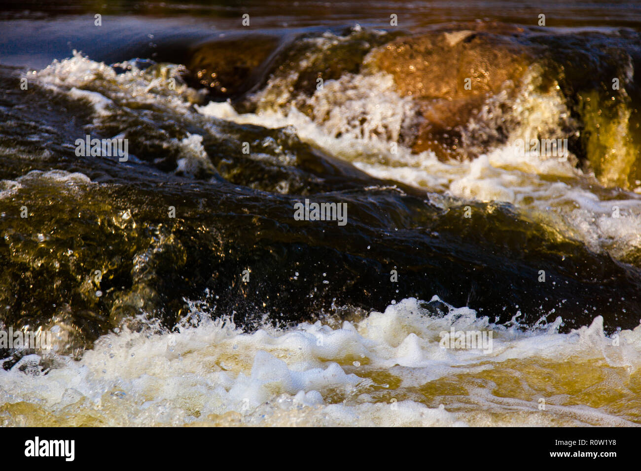 powerful stream of water goes around stone rapids with splashes and ...