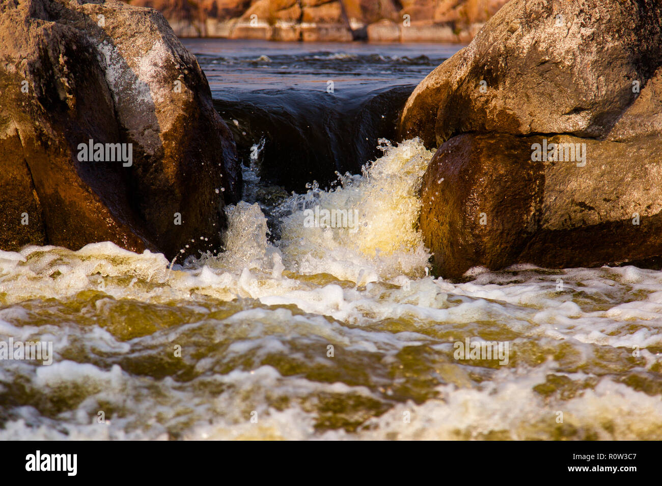 powerful stream of water goes around stone rapids with splashes and ...