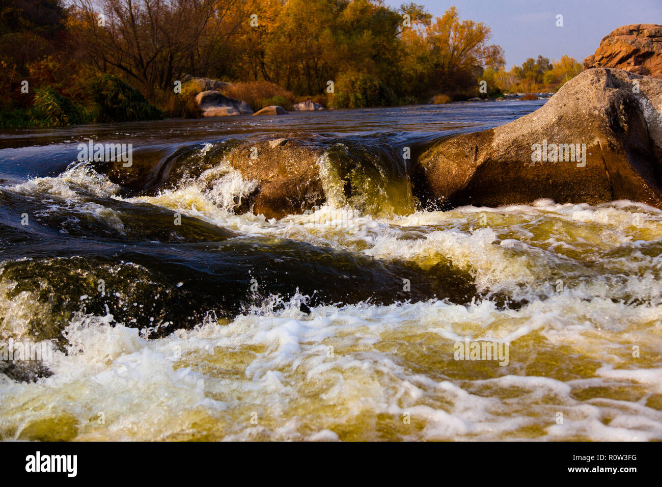 powerful stream of water goes around stone rapids with splashes and ...