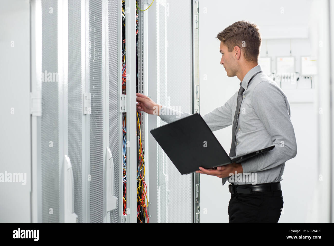 young man connecting wires in server cabinet while working with ...