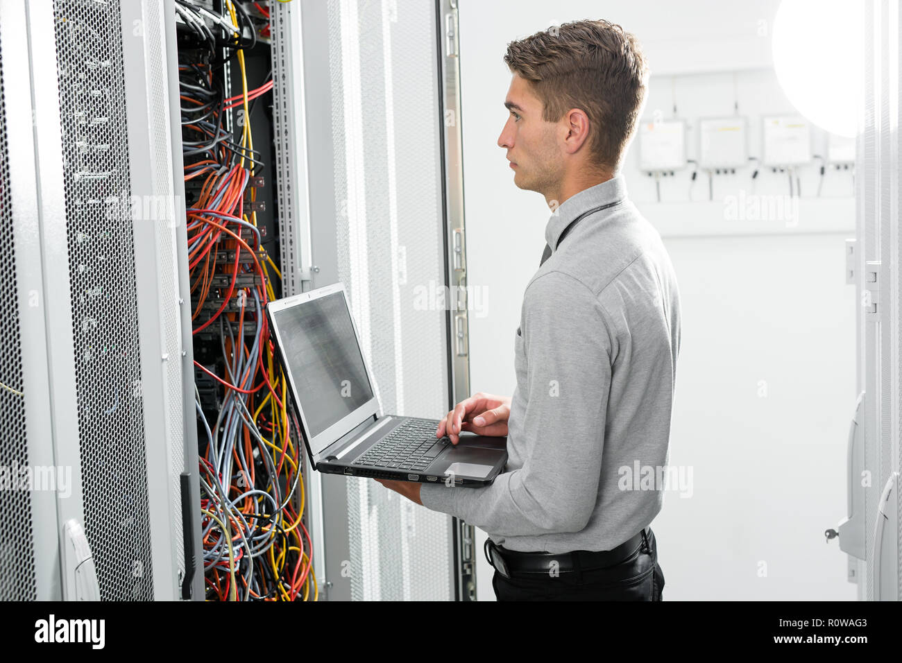 young man connecting wires in server cabinet while working with ...