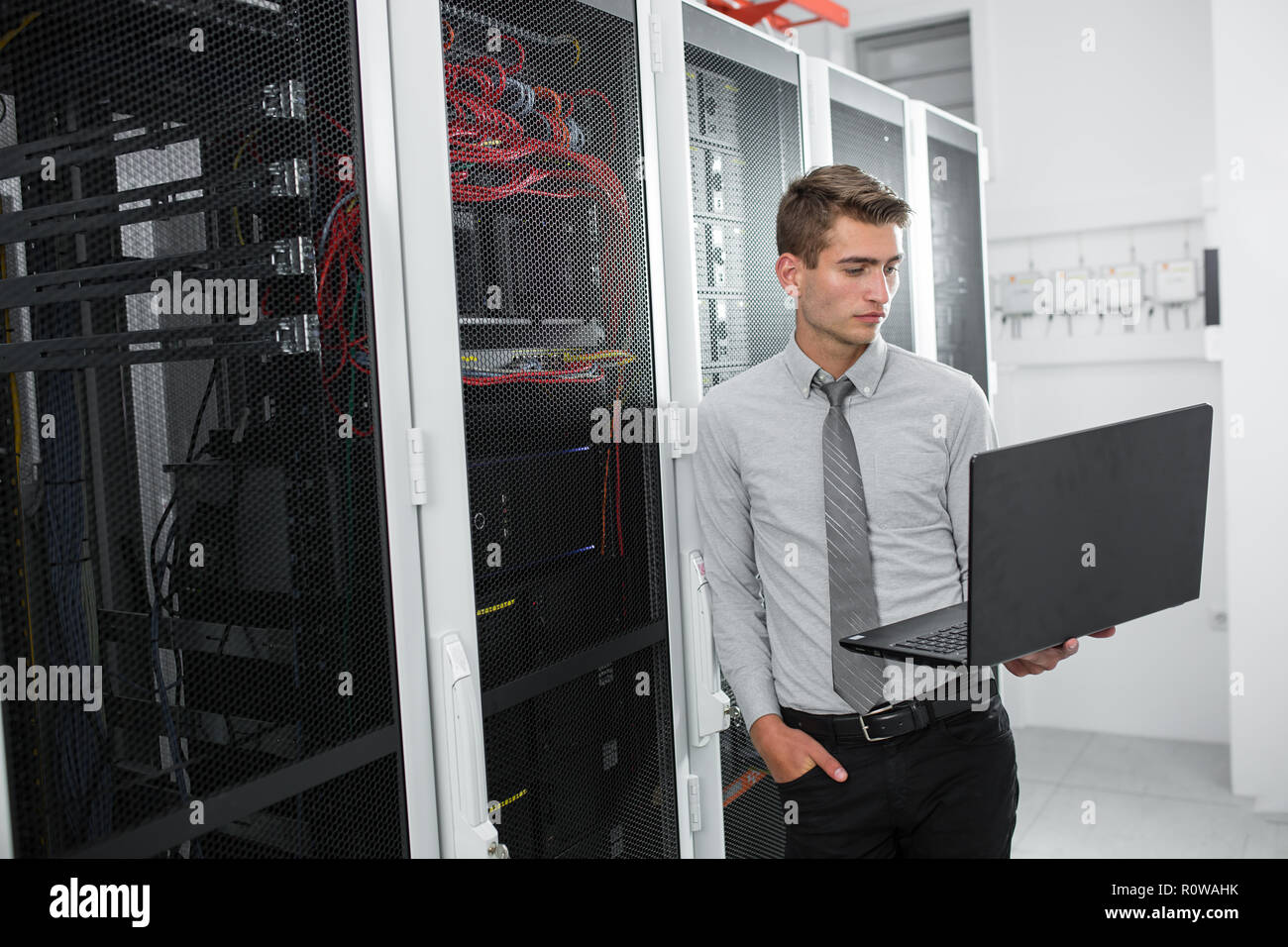young man connecting wires in server cabinet while working with ...