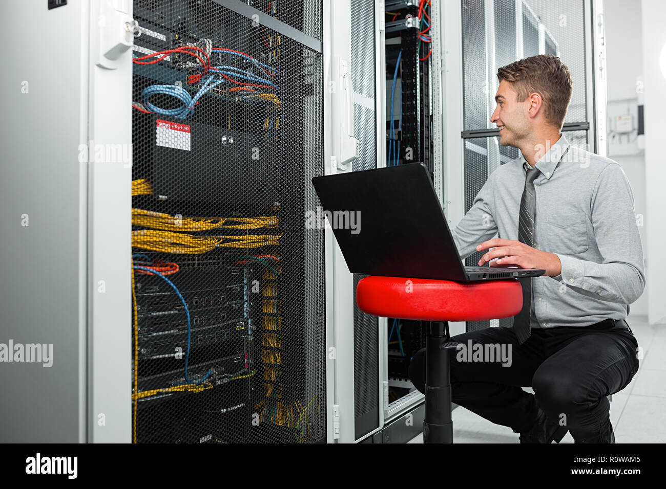 young man connecting wires in server cabinet while working with ...