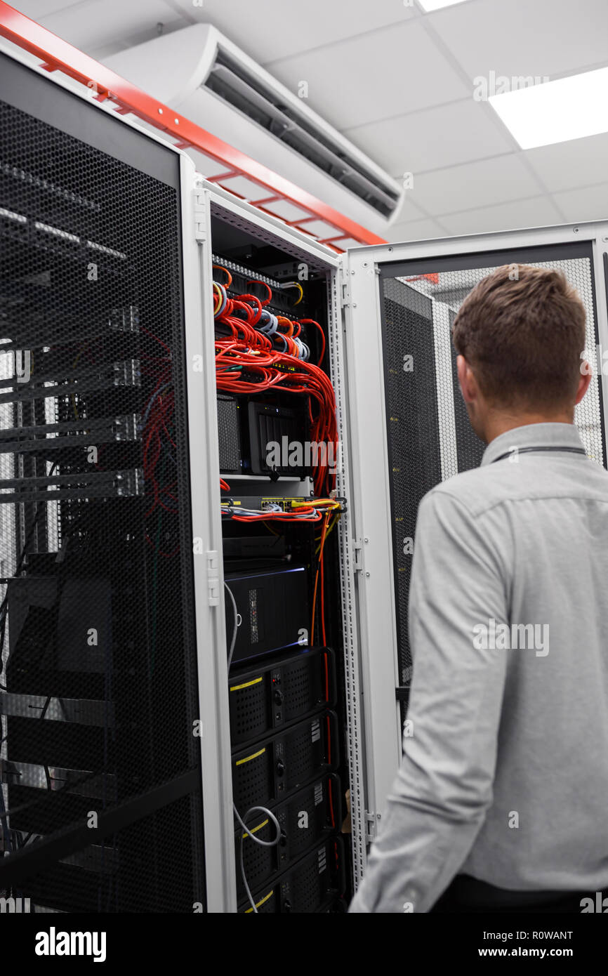 young man connecting wires in server cabinet while working with ...